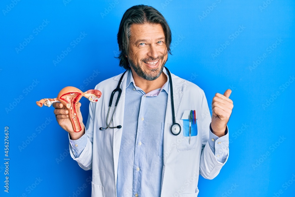 Middle age handsome gynecologist man holding anatomical model of female ...
