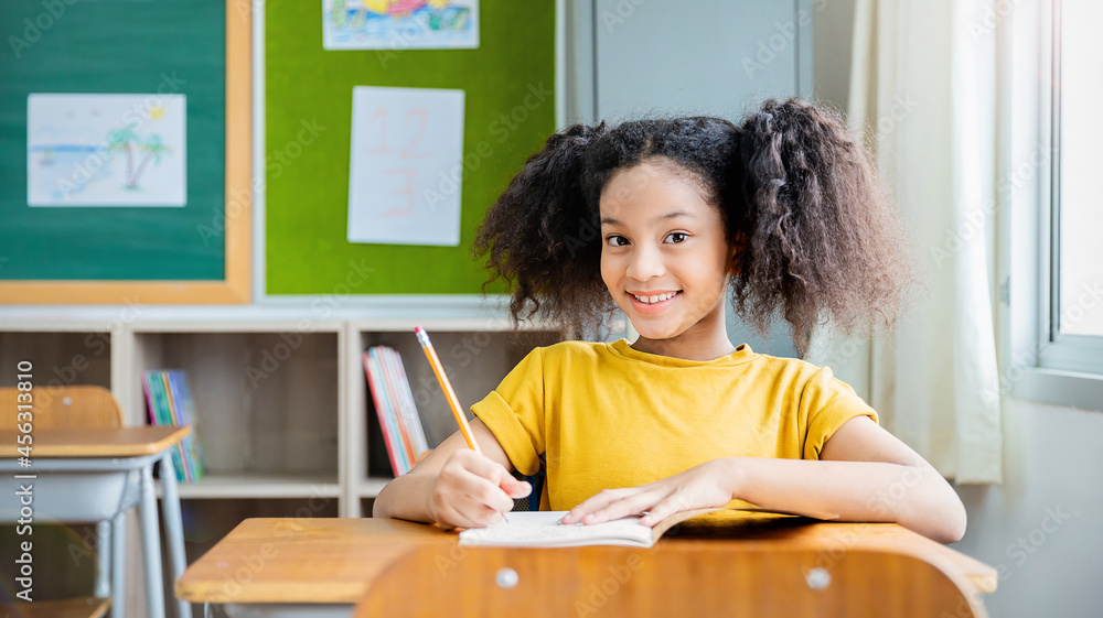 Portrait of little pupil writing at desk in classroom at the elementary ...