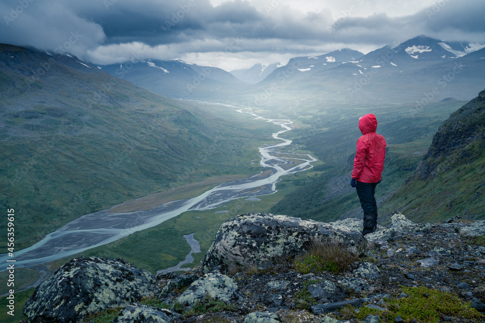 Female hiker in red jacket overlooking remote arctic valley on a cloudy ...