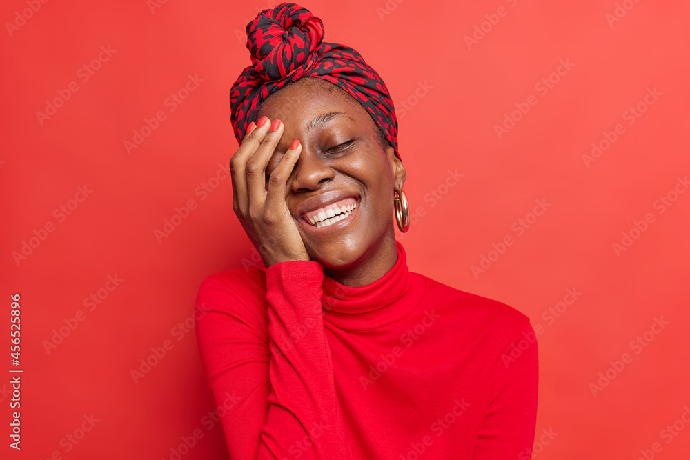 Upbeat dark skinned model keeps hand on face smiles broadly shows white ...