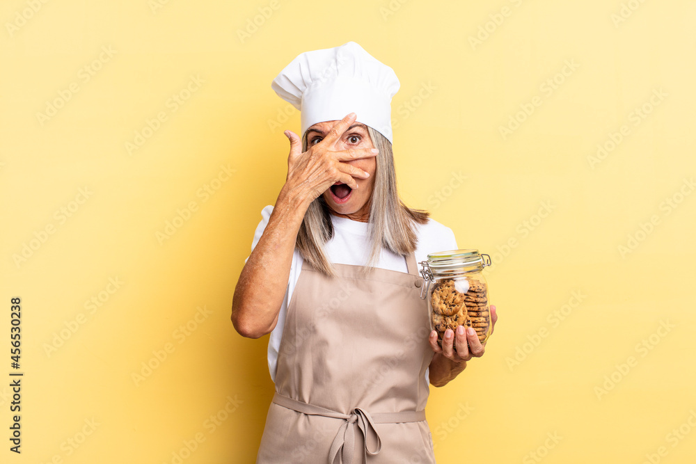 middle age chef woman looking shocked, scared or terrified, covering ...