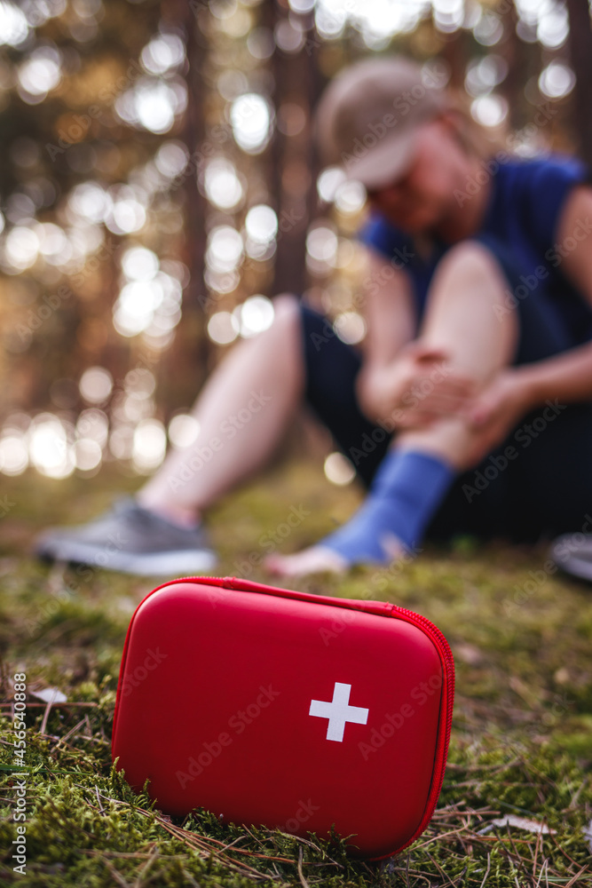 First aid kit and defocused injured tourist woman with sprain ankle in ...