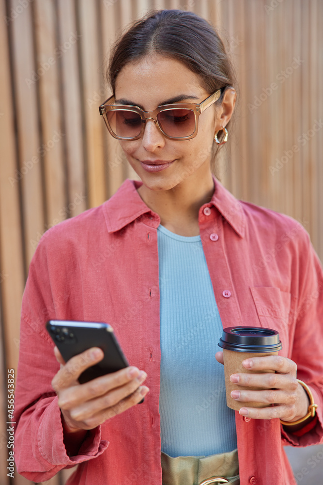 Stylish female model holds mobile phone reads notification uses online ...