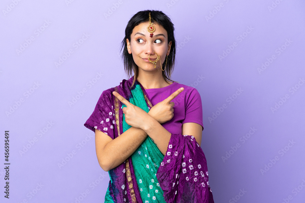 Indian woman isolated on purple background pointing to the laterals ...