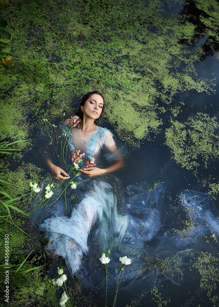 Art beautiful romantic woman lies in swamp in blue long dress with ...