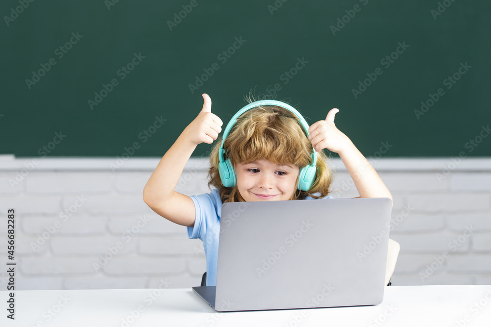 School kids with thumbs up using laptop computer and headphones in ...