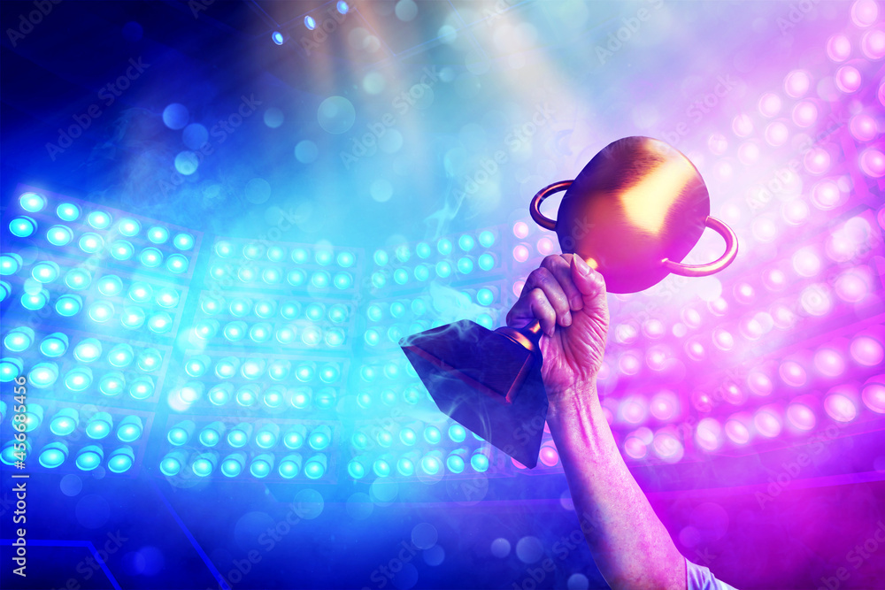 Gold trophy in winner 's hand with background spotlight on e-sport ...