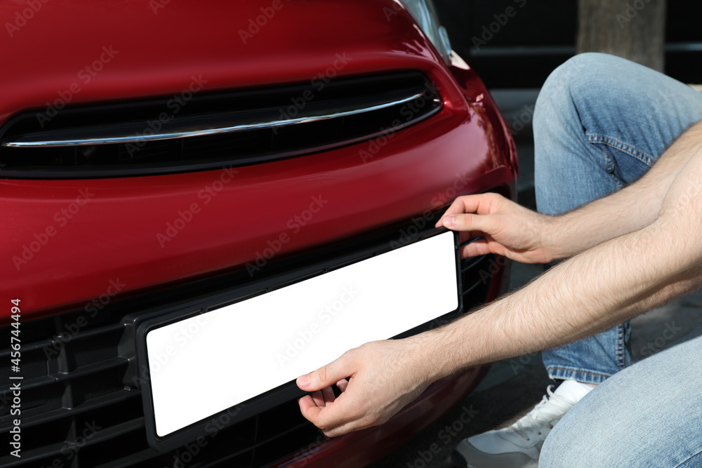Man installing vehicle registration plate outdoors, closeup. Mockup for ...