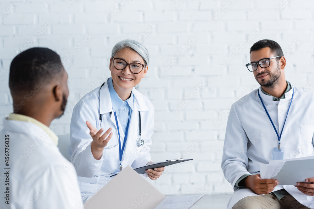 smiling asian doctor pointing at blurred african colleague during ...