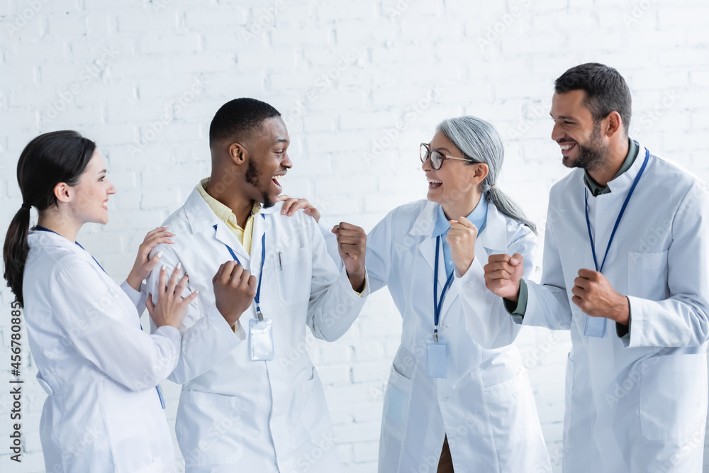 overjoyed multicultural doctors smiling at each other while showing win ...