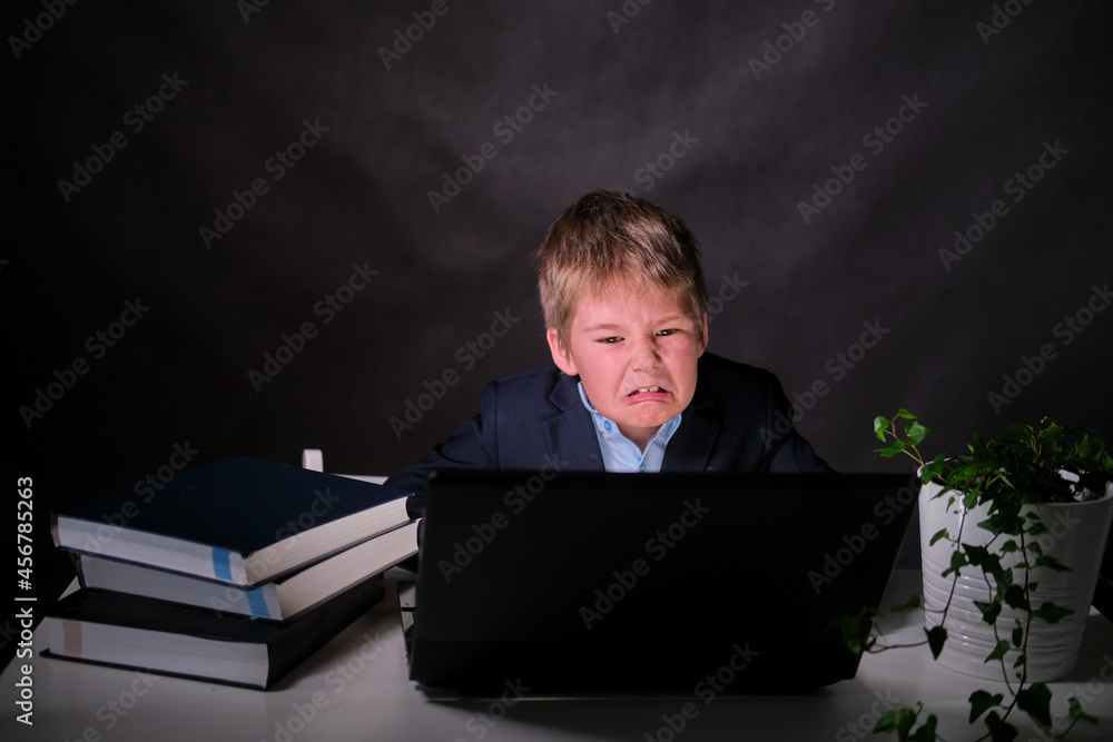 A sad boy in a school suit is crying at the computer, copy space on a ...