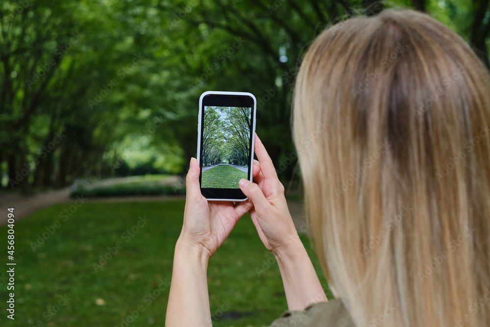 Girl holds a mobile phone in her hands and takes pictures of nature in ...
