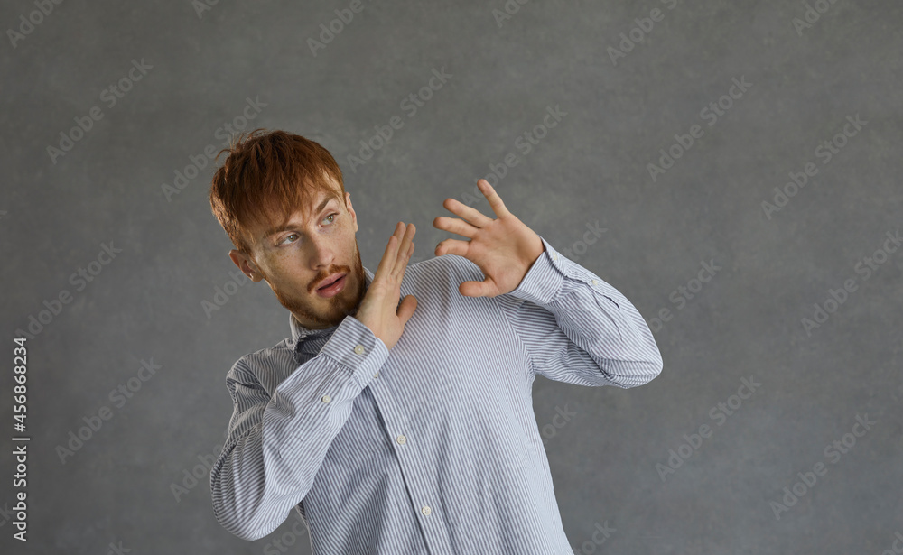 Afraid young casual man trying to protect himself with is arm standing ...