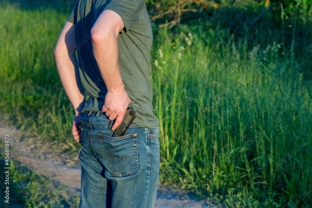 Man in green cloth holds firearm behind his back. Revolver in men's ...