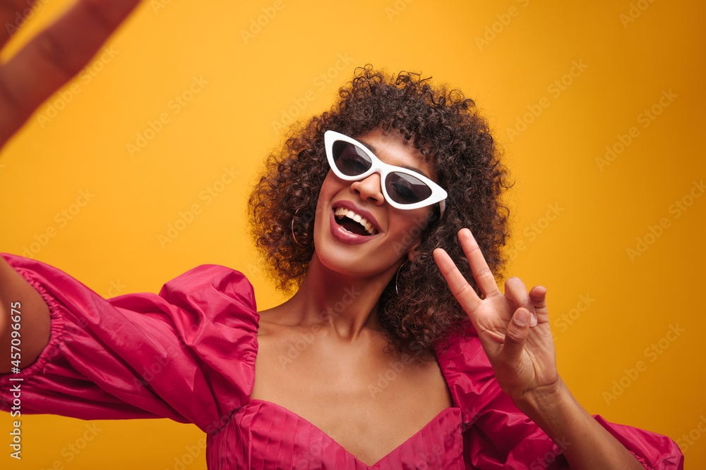 close-up of cheerful dark-skinned woman makes selfie shows index and ...
