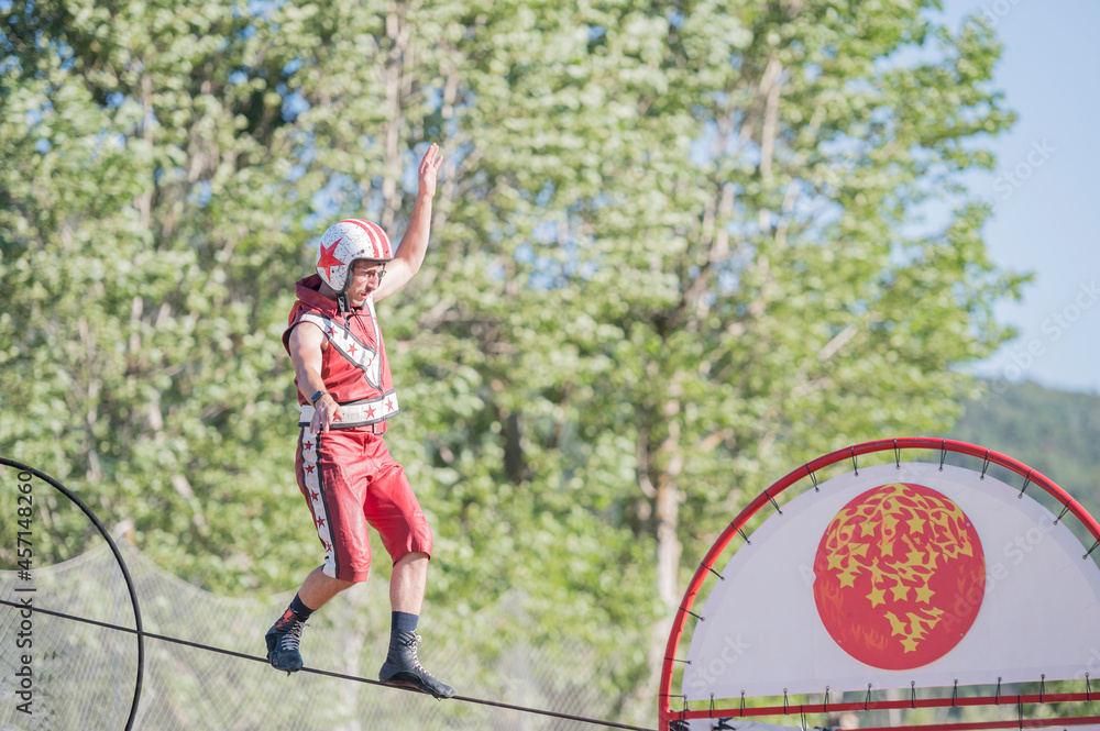 street circus. Circus person with red suit and helmet balancing on the ...