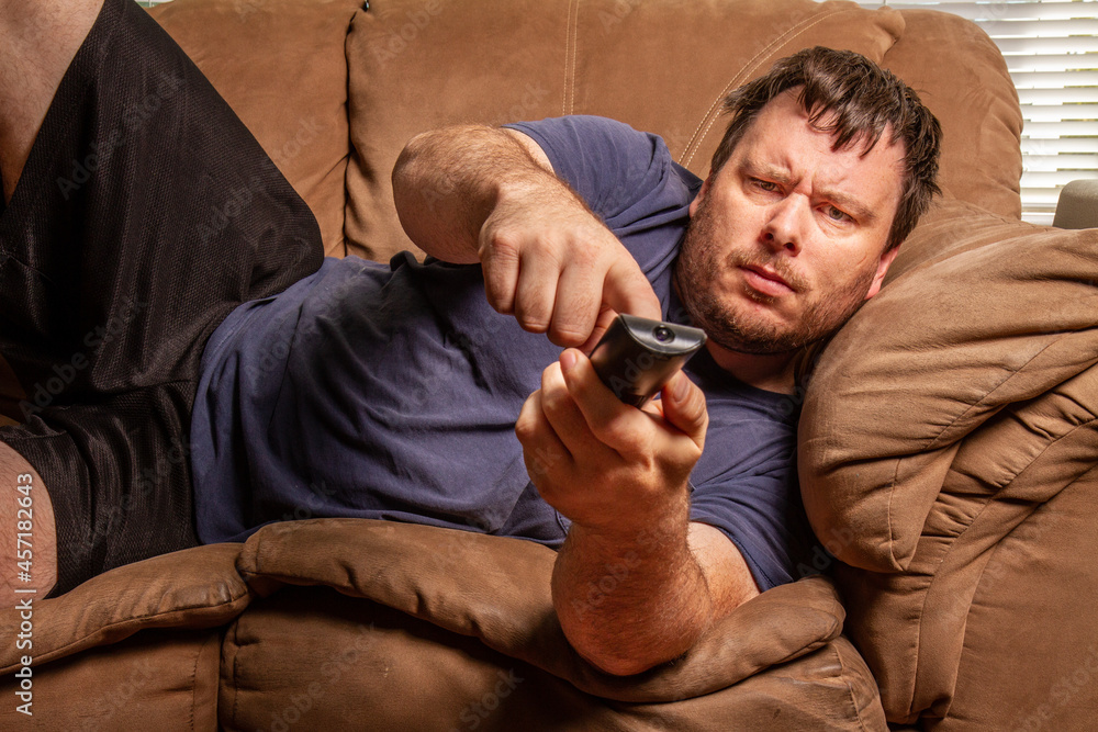 confused or angry man watching TV while pushing buttons on the remote ...