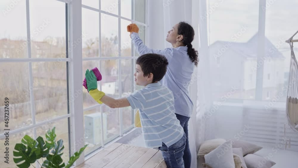 Mixed race mother with preteen son wiping window glass while little ...
