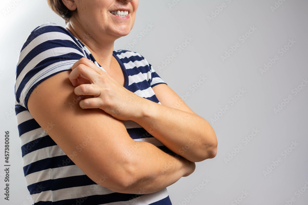 Annoyed middle-aged woman in t-shirt scratching itch on her arm, grey ...
