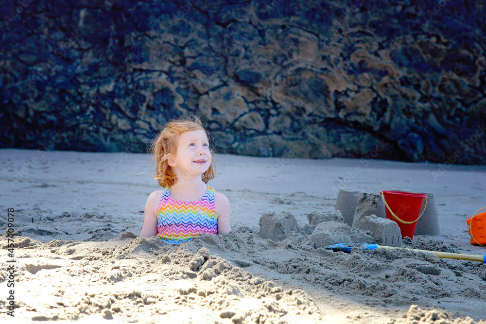 Little girl buried in the sand at the beach. ภาพถ่ายสต็อก | Adobe Stock