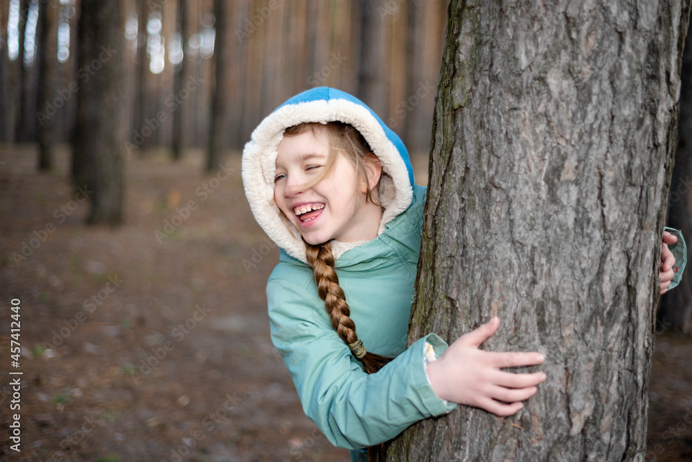 Teen girl looking out from behind the tree in the forest and laughing ...
