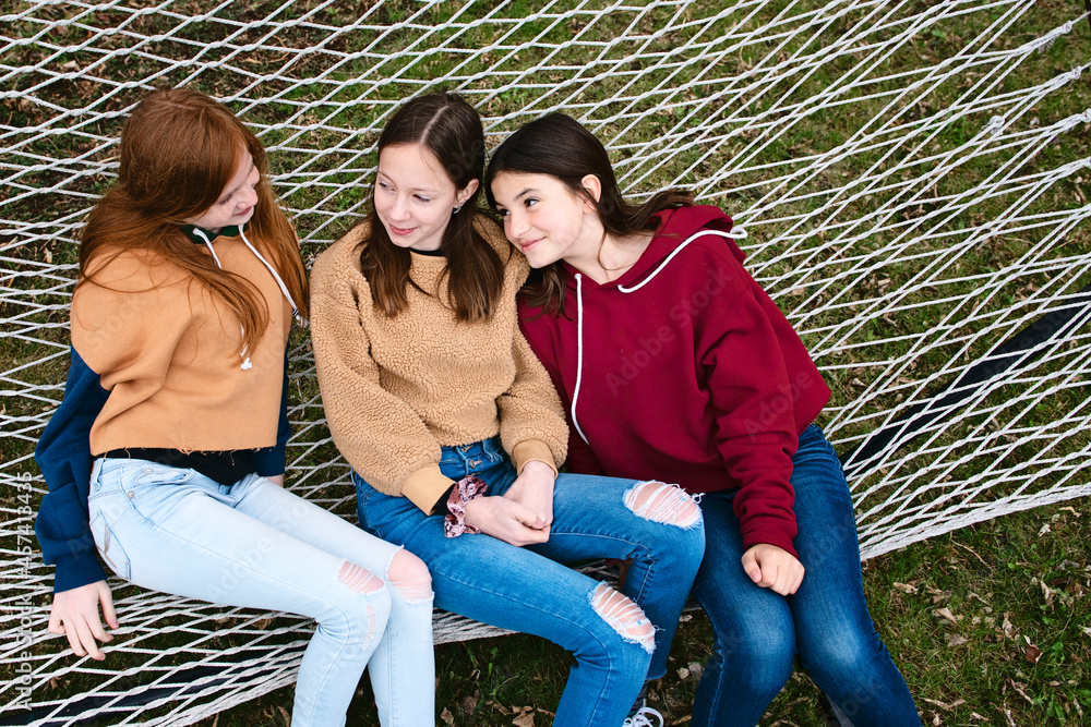 Three tween girls sitting on a hammock together talking. Stock Photo ...