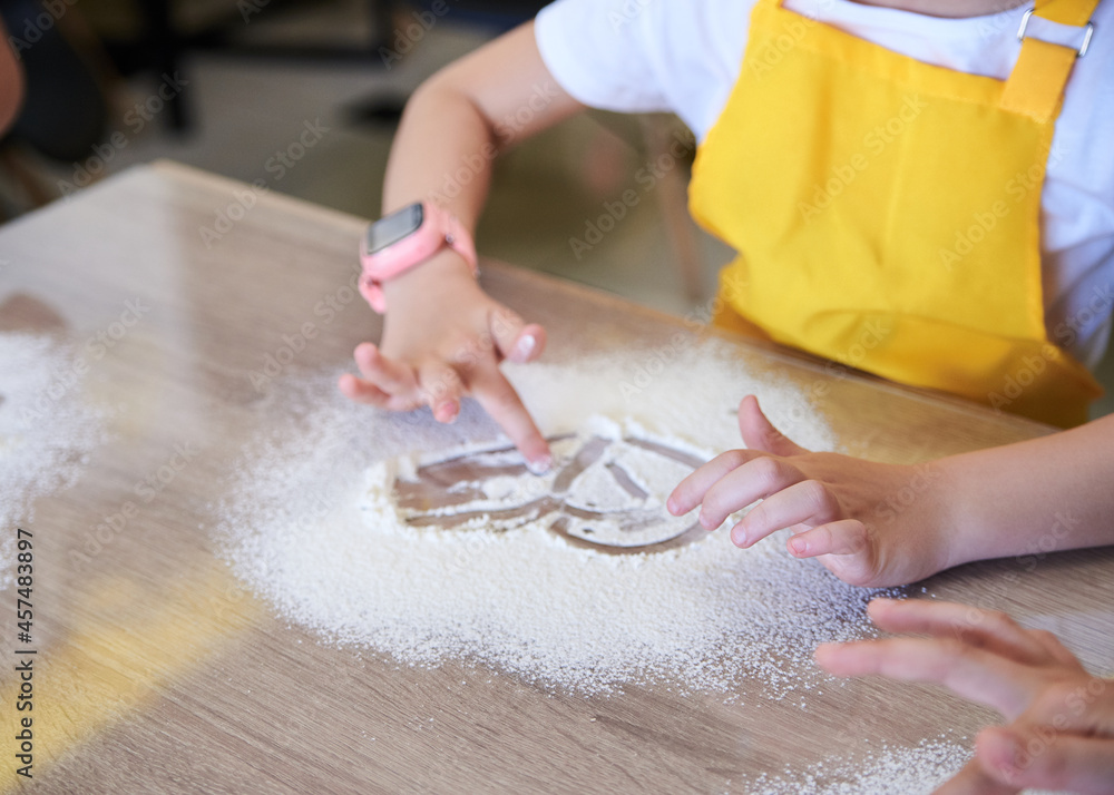 Child wearing yellow apron, playing with flour on table. Close-up ...