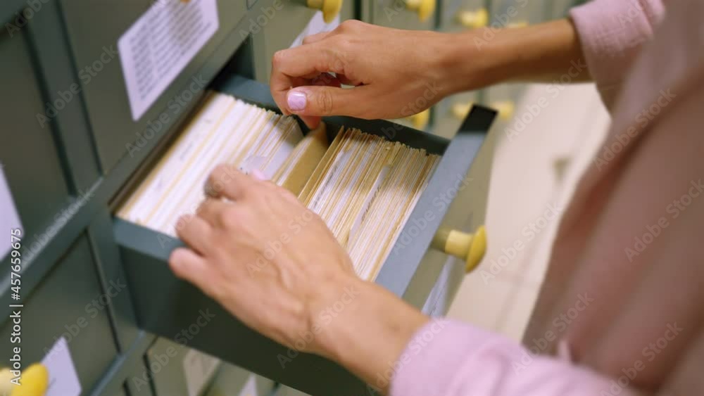 A woman hand searching cards in old wooden card catalogue. A vintage ...