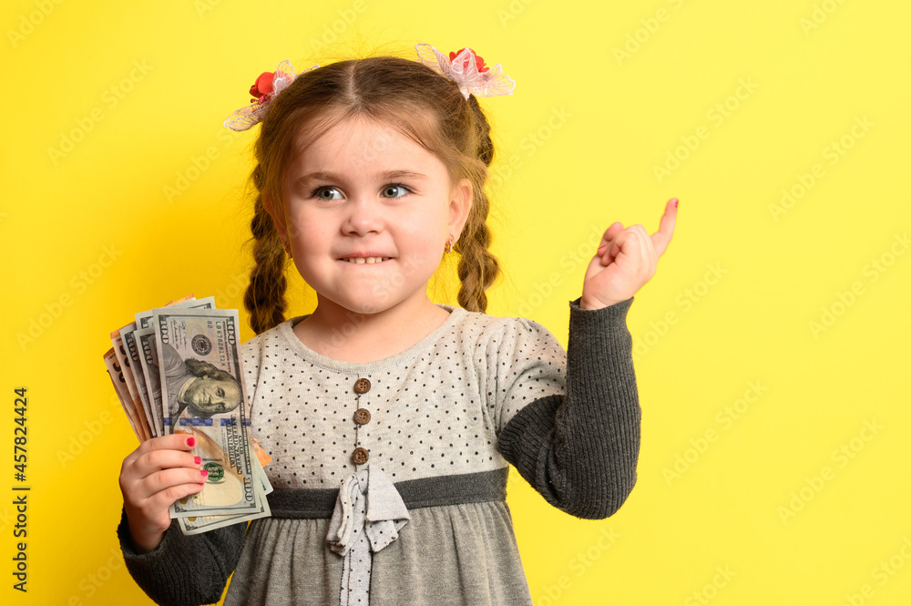 Caucasian girl holding money, portrait of a child on a yellow ...