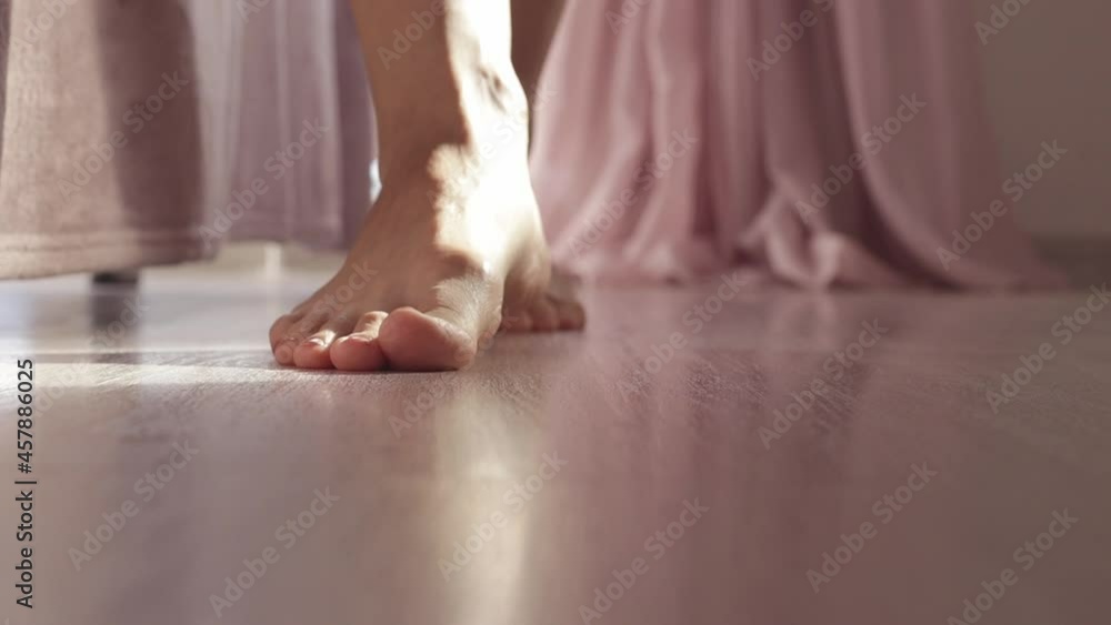 Female bare feet walk across the floor from window to camera. Close up ...