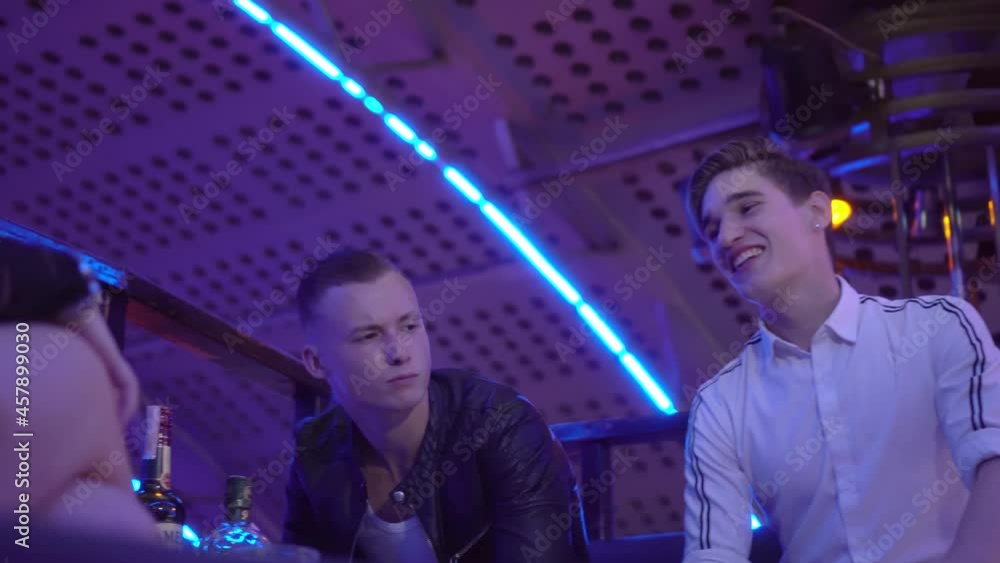 Guys and girls relax at a table in a nightclub. They laugh, drink, talk ...