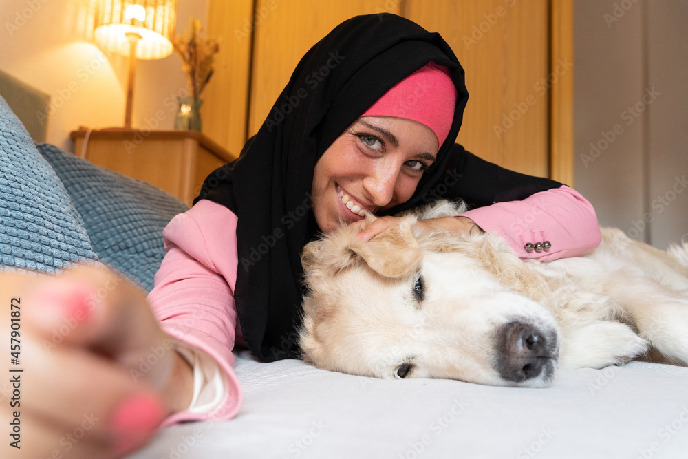 Cheerful muslim woman with pet wearing a hijab indoors. Horizontal side ...