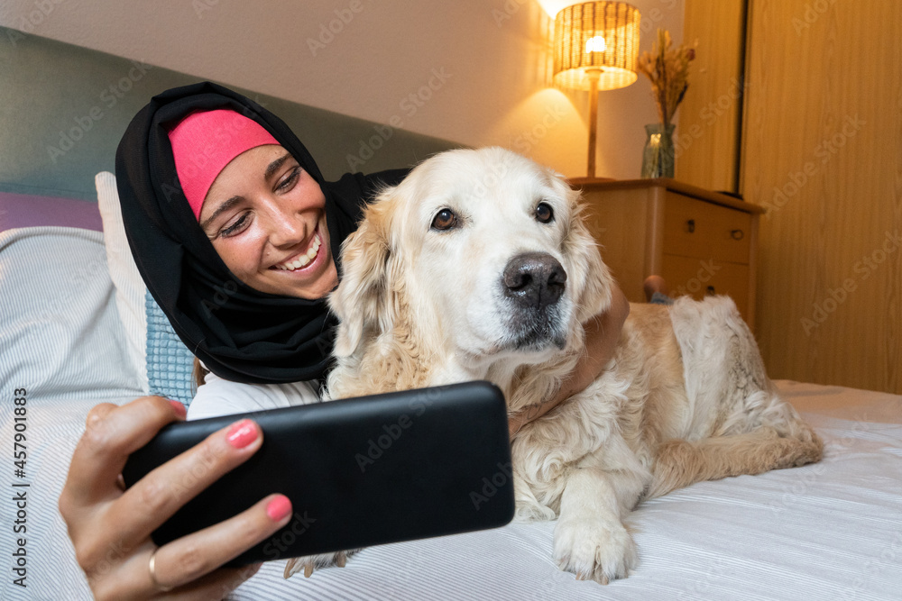 Cheerful muslim woman wearing a hijab using smartphone indoors ...