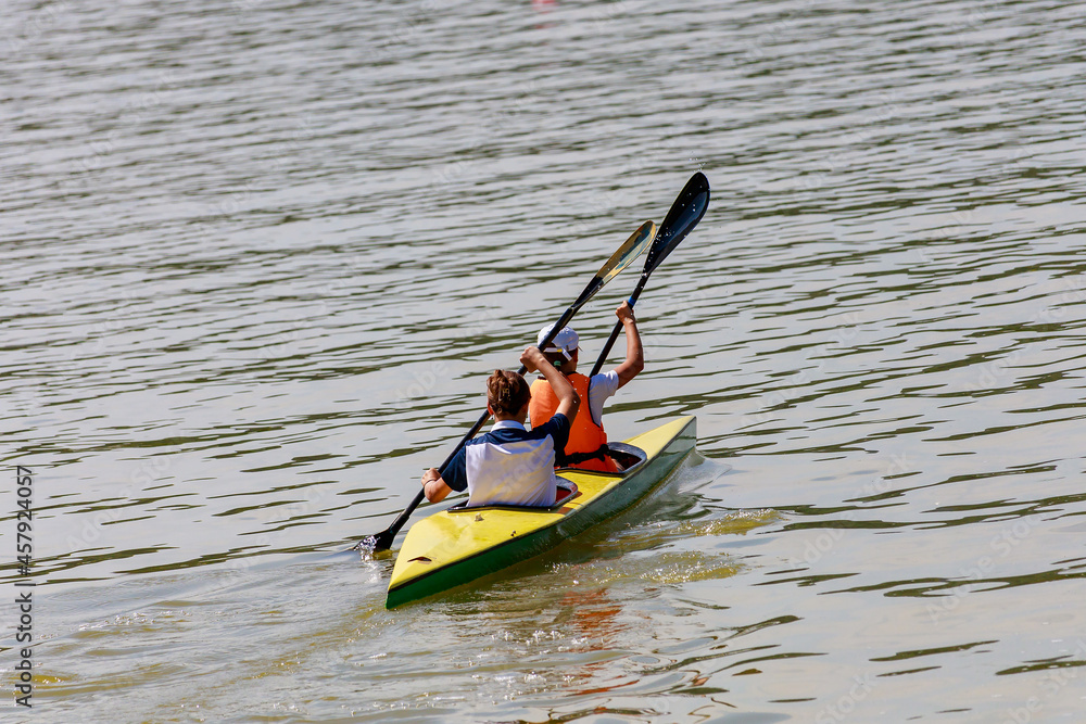 Two girls with oars are rowing synchronously on a kayak on the river ...