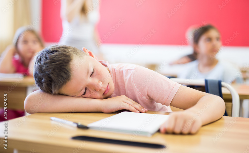 Tired little boy lying on work desk put head on his hand, feel ...