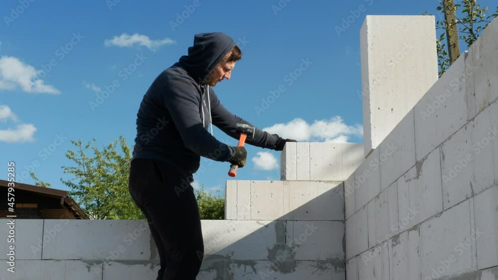 A young builder is building a house with his own hands. Bricklayer lays ...