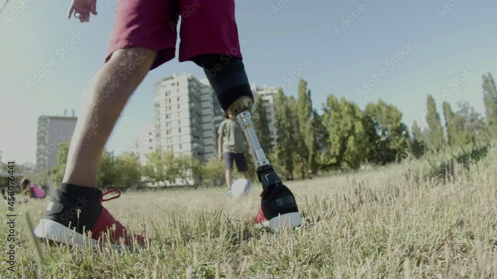 Close-up of mans prosthetic leg kicking ball around. Disabled father ...
