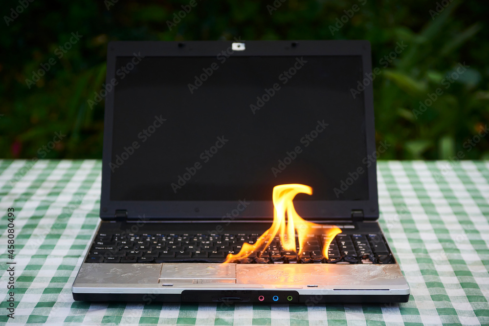 Laptop burning in flames on a desk, fire hazard. losing valuable data ...