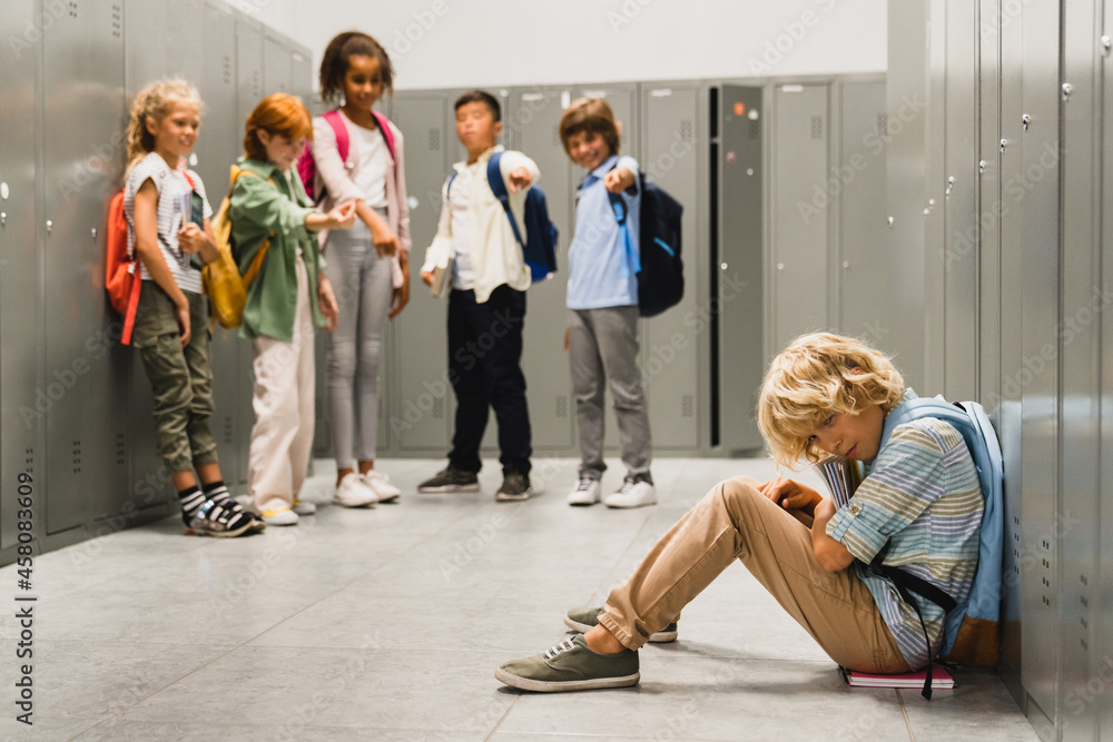 Sad crying schoolboy pupil sitting on the floor at the school hall ...