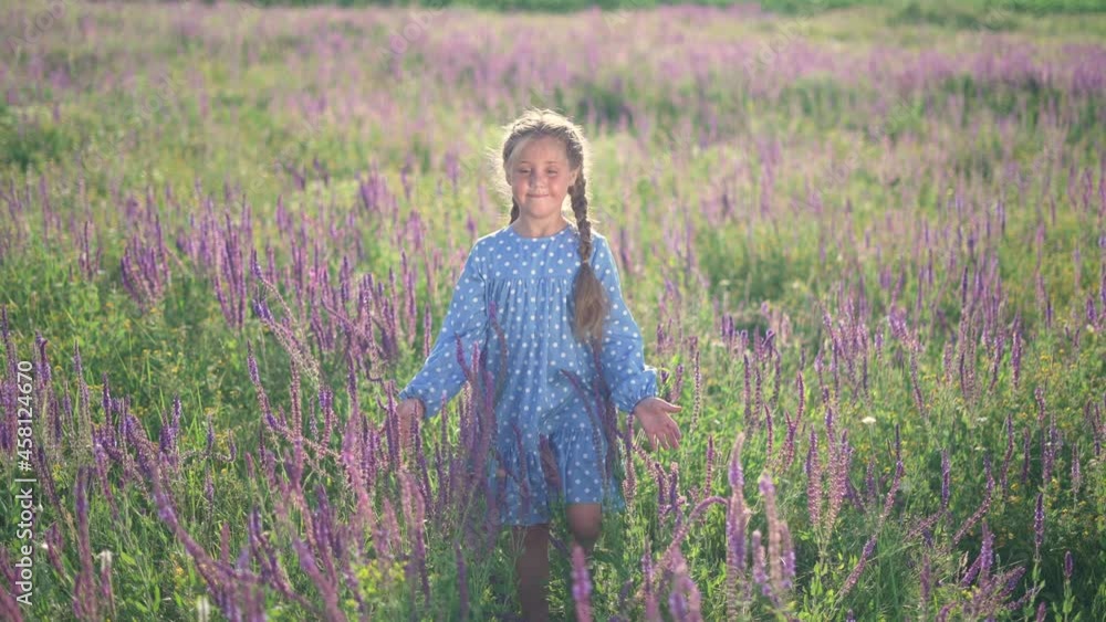 Girl in flower field. Child touches blue flowers with his hand. Girl in ...
