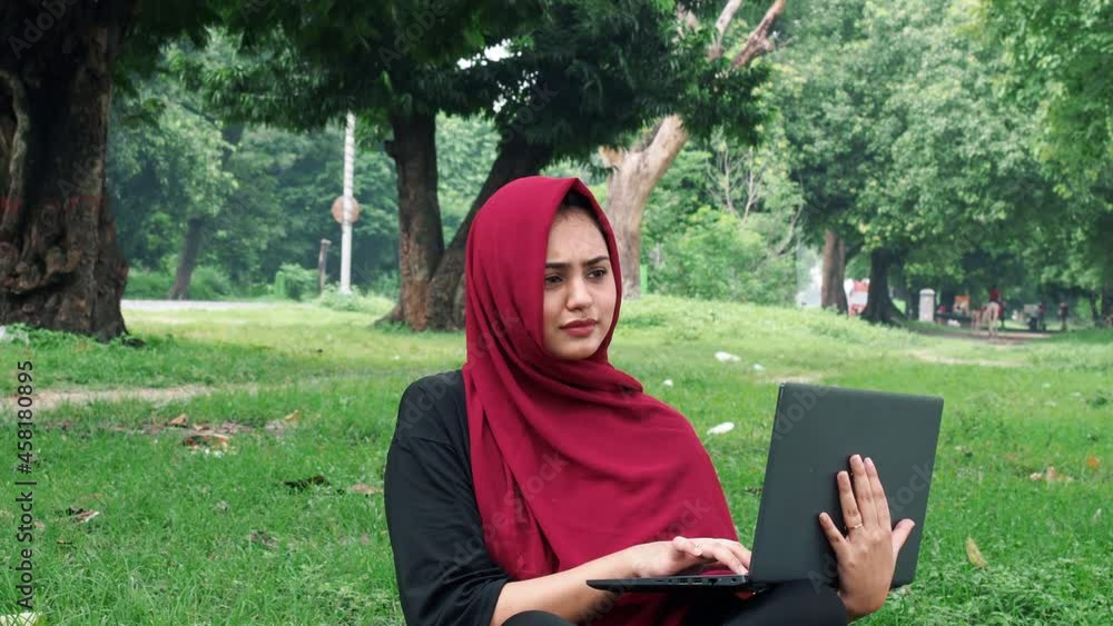 Happy Afghan woman in hijab working on laptop computer on green lawn ...