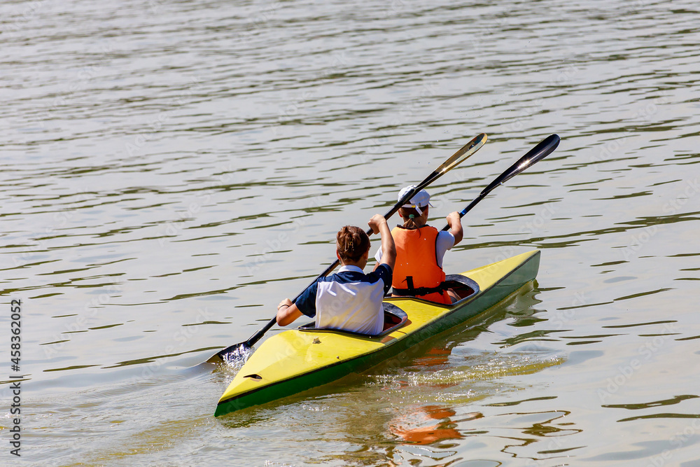 Two girls with oars are rowing synchronously on a kayak on the river ...