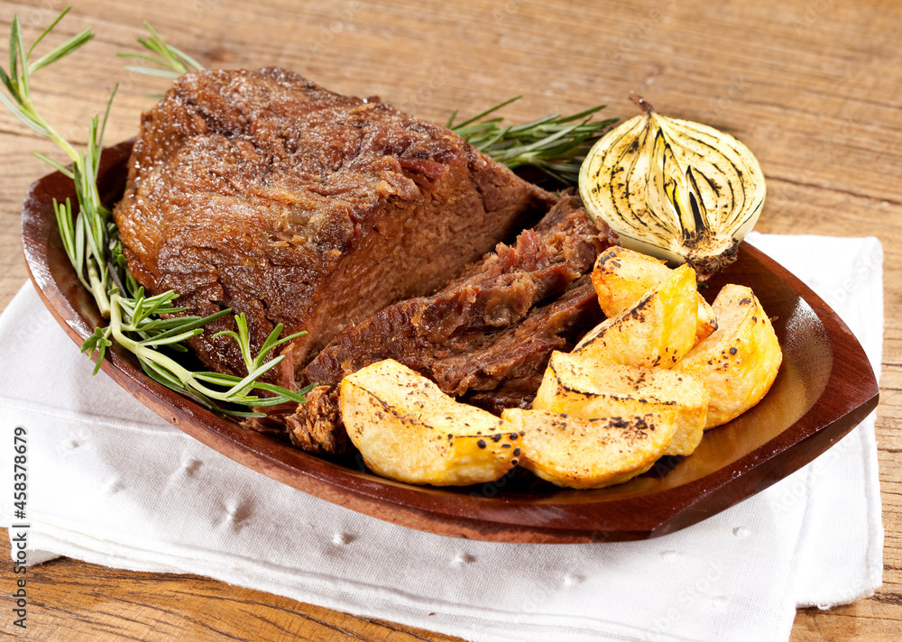 Foto de Carne assada com batatas na travessa de madeira no fundo de ...