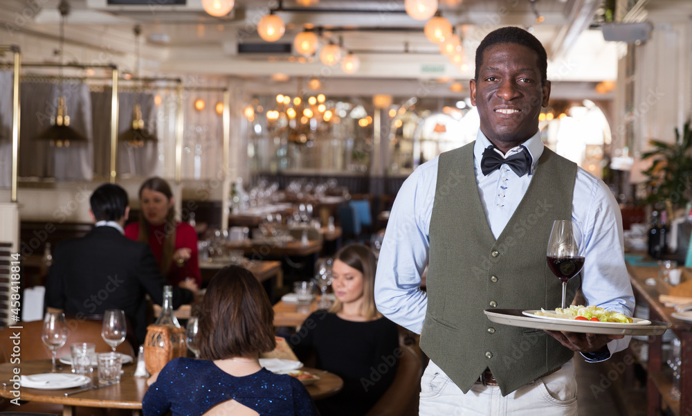 Hospitable African American waiter standing with serving tray ...
