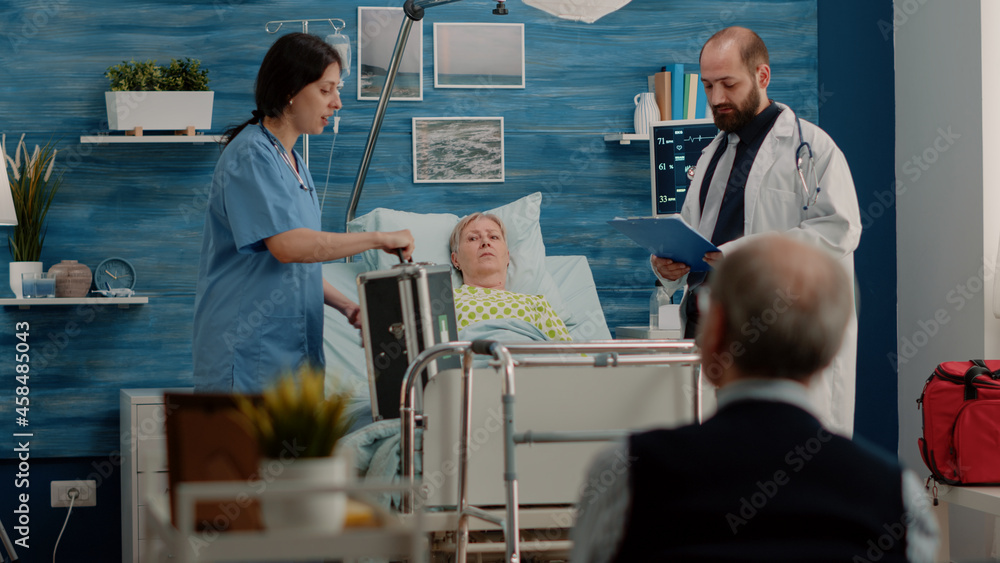 Doctor and nurse doing checkup visit for ill patient in hospital bed ...