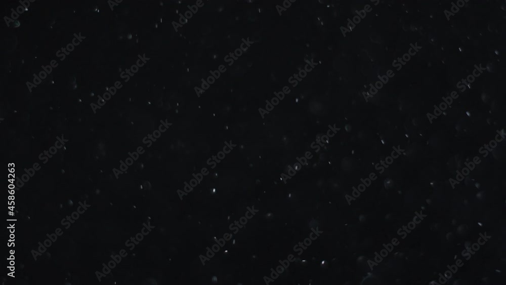 A suspension of white-silver particles in the air on a black background. Some of the particles ...