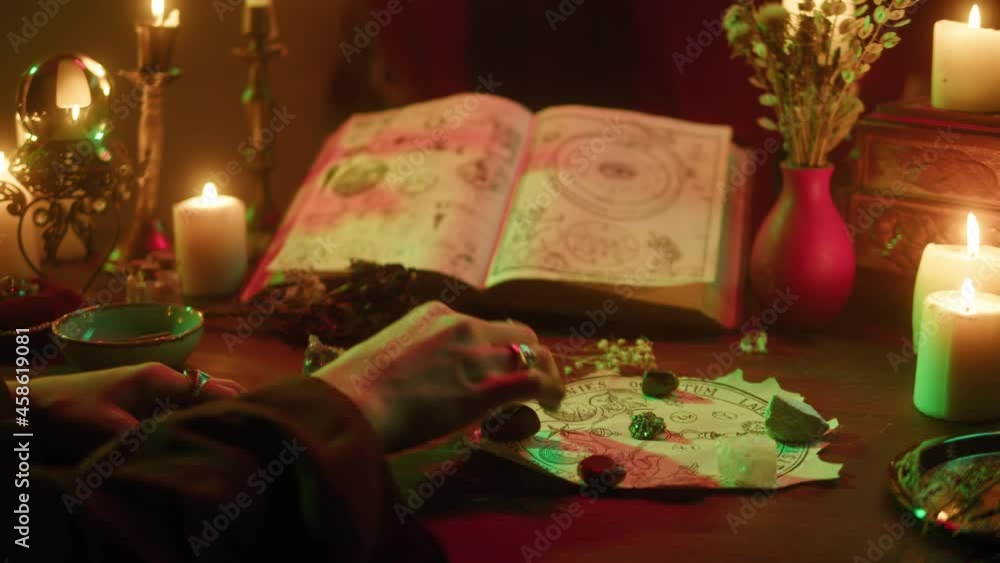 Witch putting magical stones close-up. Table with spellbook for making ...