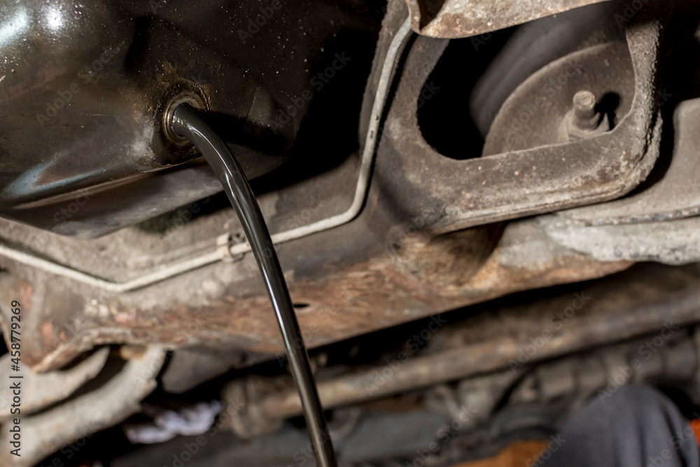 Old And Dirty Oil Is Drained From The Underchassis Of An SUV old-and-dirty-oil-is-drained-from-the-underchassis-of-an-suv