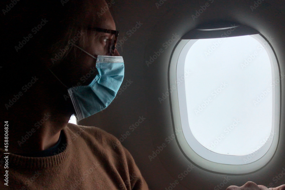 Man wears a face mask and look the sky by an airplane window, pandemic ...