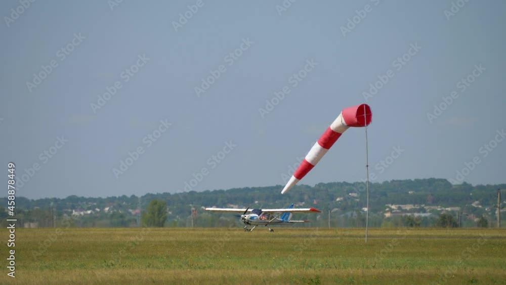 Striped windsock swings in wind on blue sky background. Red white cone ...